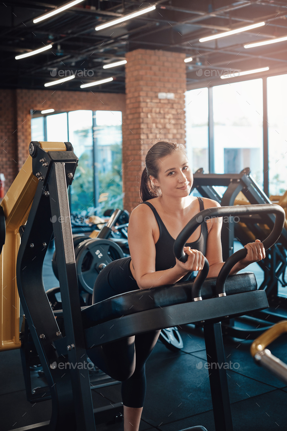 Serious female sportsperson looks at camera posing on training machine ...