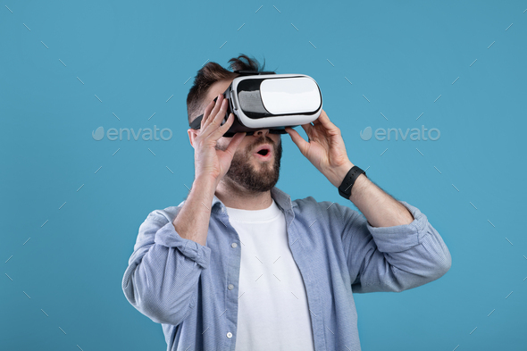Cool millennial guy experiencing virtual reality in VR headset on blue ...