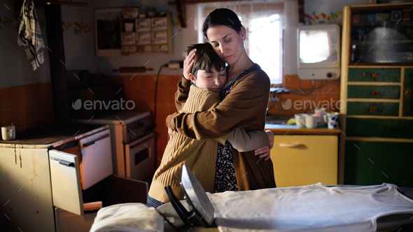 Portrait of sad poor mature mother hugging small daughter indoors at ...