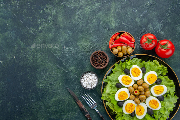 top view boiled sliced eggs consists of green salad and olives on dark ...