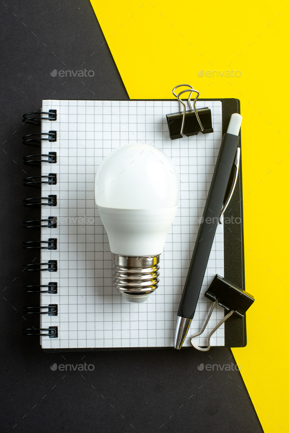 Vertical view of lightbulb spiral notebook on book and pens on black ...