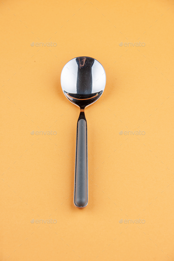Vertical view of stainless teaspoon lying on golden background with ...