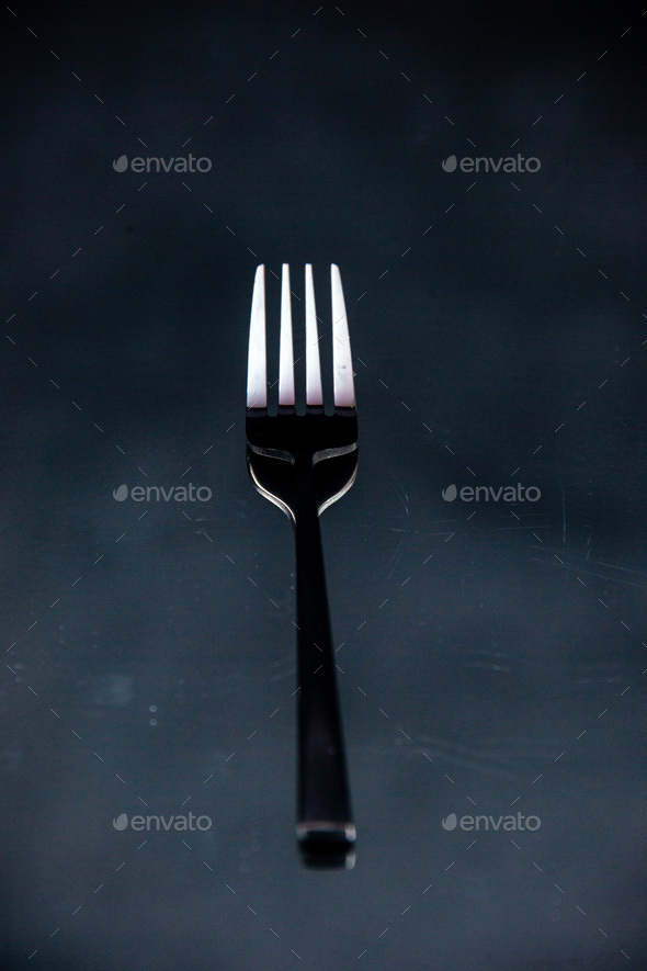 Overhead view of elegant shiny metal fork on black wave background with ...