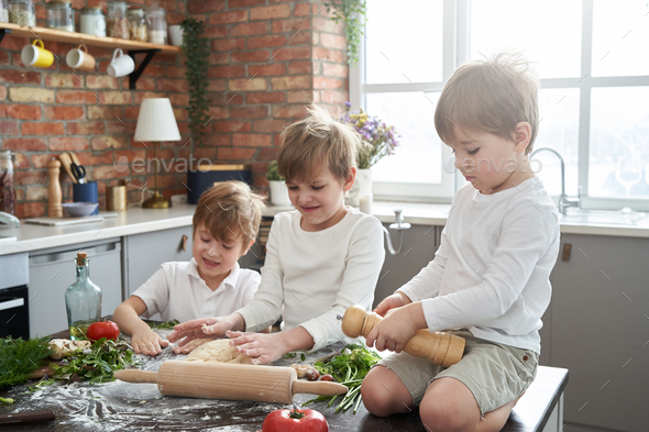 Caucasian little brothers cooking a pizza together in modern kitchen ...