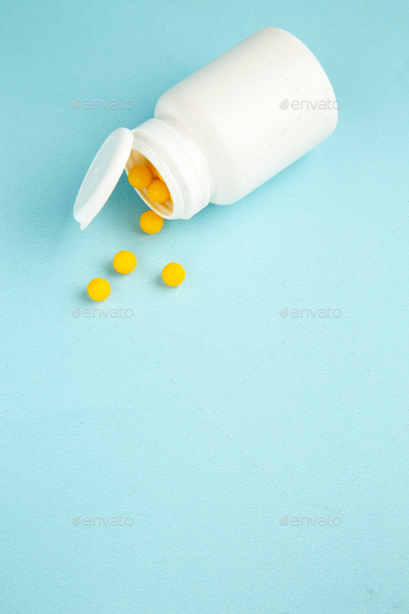 above view little pill can with yellow vitamine pills on blue ...