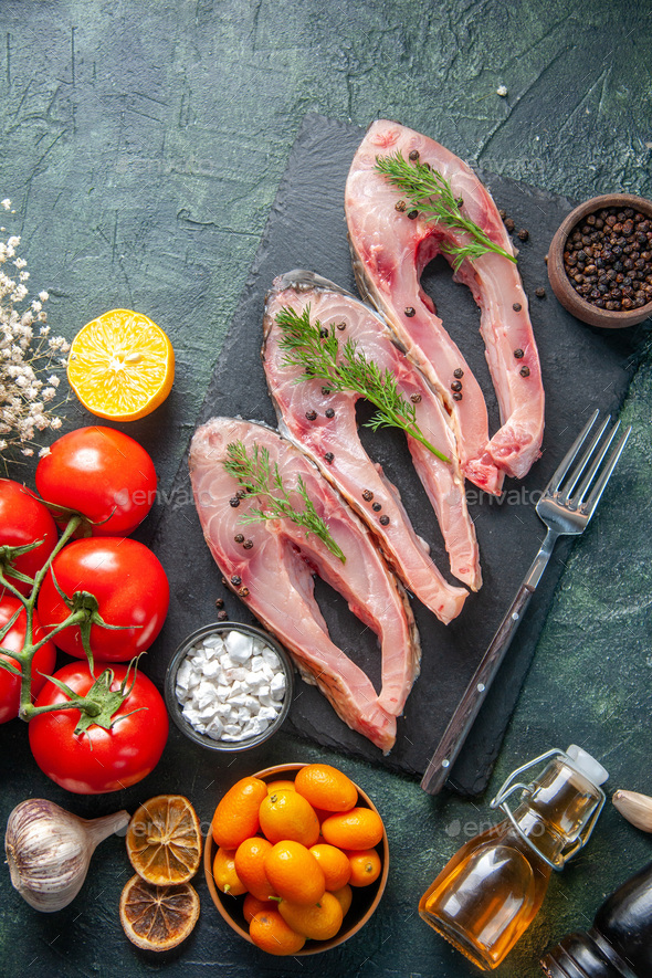 top view fresh fish slices with red tomatoes and kumquats on dark ...