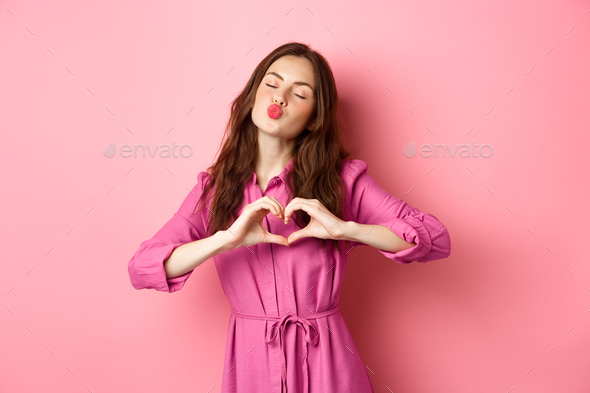 Beautiful romantic girl smiling, showing heart gesture, standing in ...