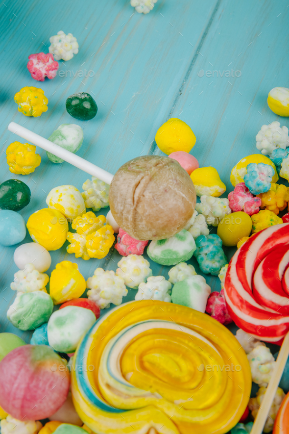side view of lollipop candies and colorful candies scattered on blue ...