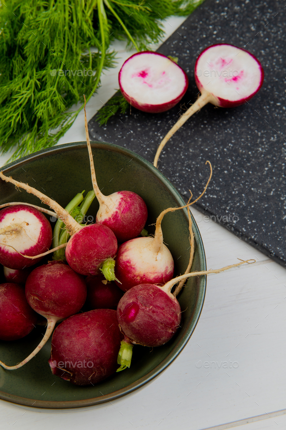 side view of bowl full of radish with half cut one on cutting board and ...