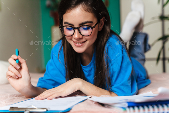 Lovely smart young girl studying while laying i Stock Photo by vadymvdrobot