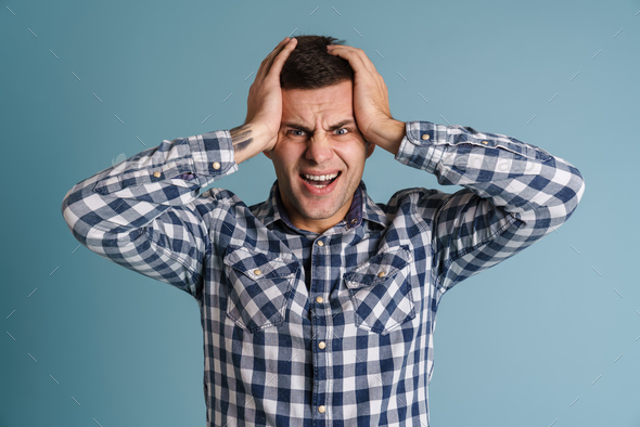 Angry young man screaming isolated over blue Stock Photo by vadymvdrobot
