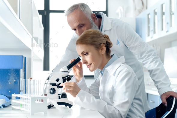 focused caucasian scientists in white uniform working with microscope ...