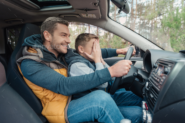 smiling father teaching scared little son driving car in forest Stock ...