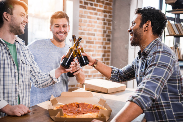 Group of happy young people having fun with beer and pizza at home ...