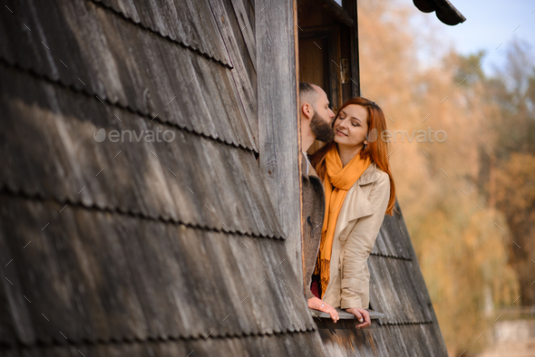 Happy young family peeking out of the windows of a large wooden house ...