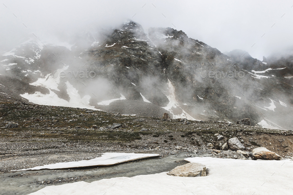 Mountain landscape with rocks and creeping fog. High snow peaks in the ...