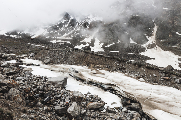 Mountain landscape with rocks and creeping fog. High snow peaks in the ...