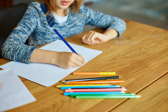 School girl drawing and writing a picture with crayons, using colored ...