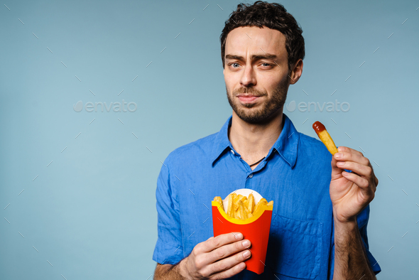 Confused handsome guy eating french fries with ketchup Stock Photo by ...