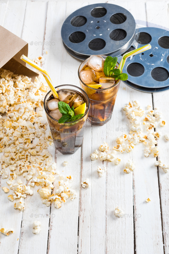 Close-up view of popcorn with iced tea in glasses and film reels on ...