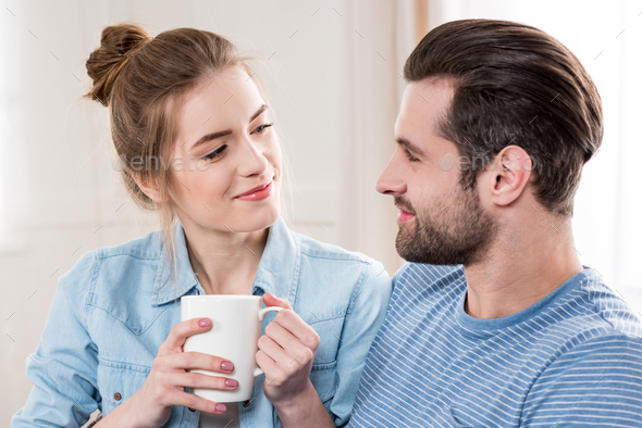 Beautiful young couple drinking tea and looking at each other at home ...