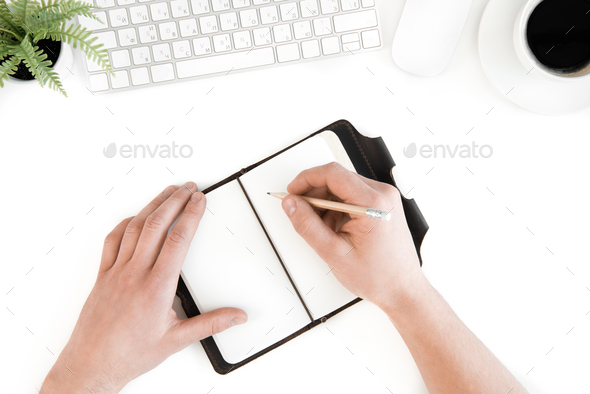 top view of person writing in diary at workplace with computer keyboard ...