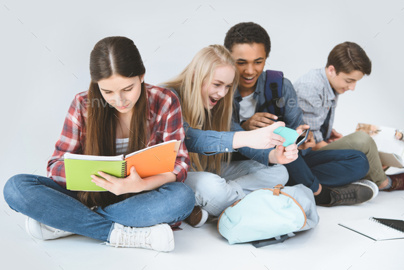 students doing homework while multiethnic friends using smartphones ...