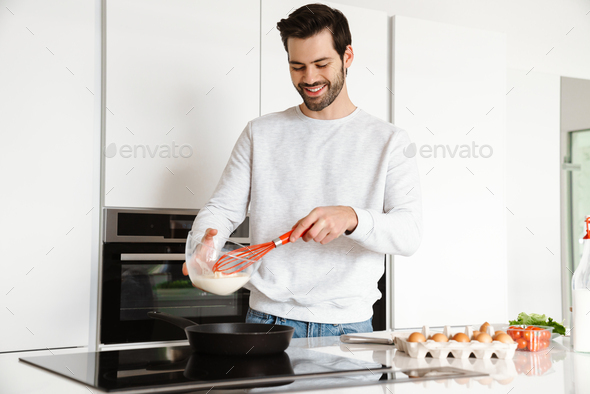 Happy handsome young man smiling while cooking scrambled eggs Stock ...