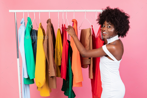 African Lady Picking Clothes Posing Near Clothing Rail, Pink Background ...