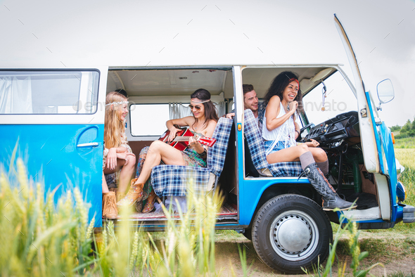 Happy friends driving a vintage minivan Stock Photo by oneinchpunchphotos