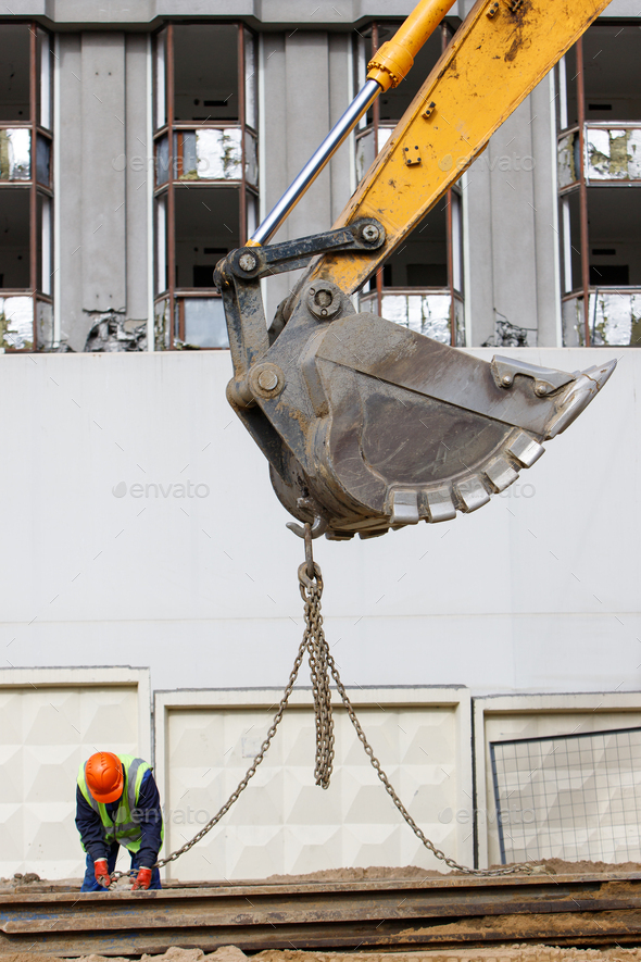 Excavator bucket lifting metal beam with worker helping Stock Photo by ...