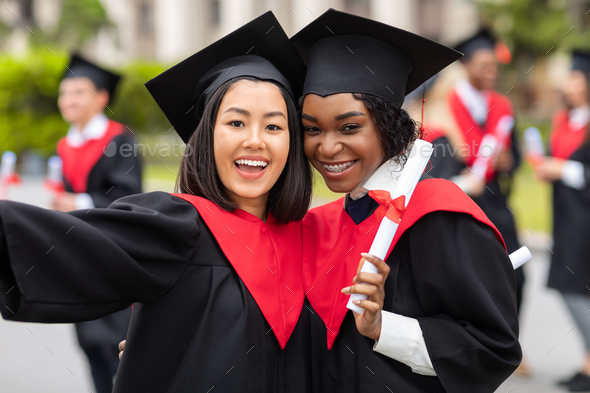 Cheerful young ladies in graduation robes taking selfie Stock Photo by ...