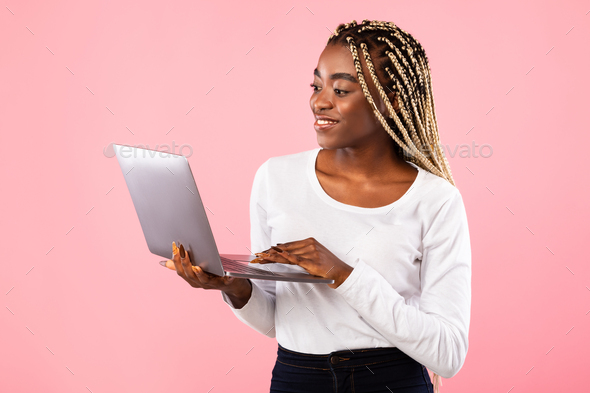 Smiling young black lady holding and using laptop Stock Photo by ...