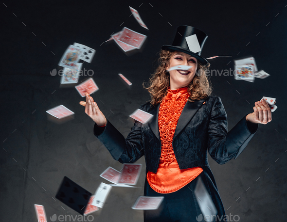 Funny female rogue from circus poses with flying cards in dark ...