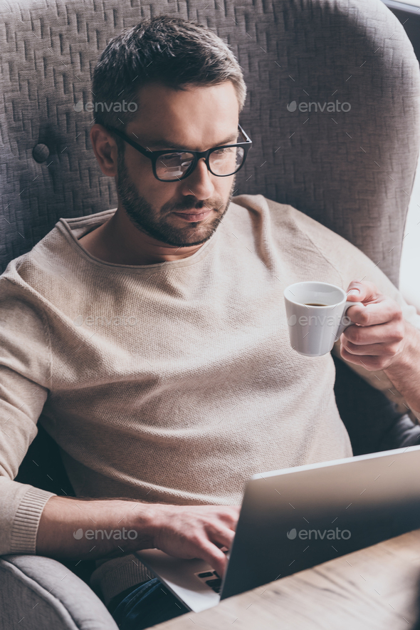 Concentrated on work. Handsome man using his laptop and holding coffee ...