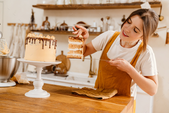 Beautiful happy pastry chef woman showing piece of cake with cream ...