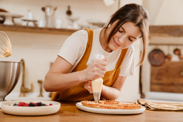 Beautiful happy pastry chef woman smiling while making tarts with cream ...