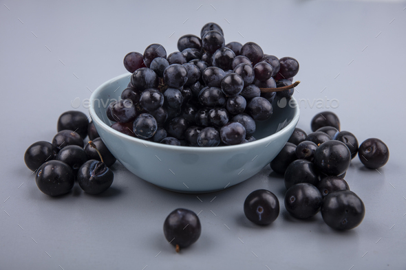 side view of fruits as grape in bowl and sloe berries on gray ...