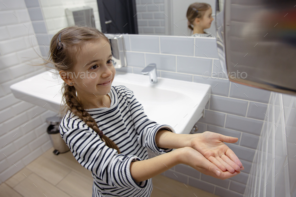 Little girl in the bathroom dries her hands with a hand dryer. Stock ...