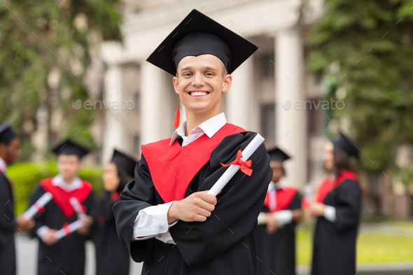 Cheerful guy in graduation costume with diploma posing outdoors Stock ...