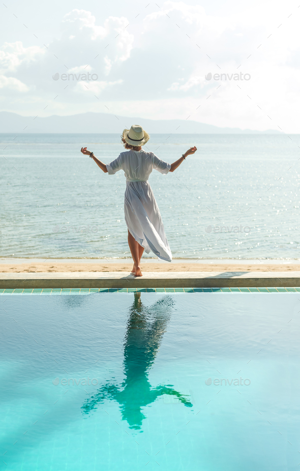 back view of girl standing at swimming pool and looking at the ocean ...