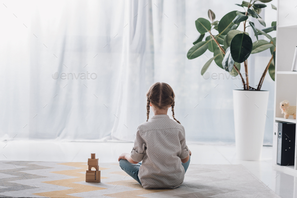 rear view of little child sitting on floor with wooden blocks and ...