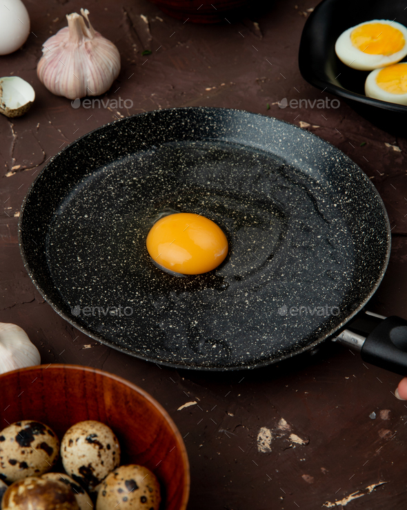 side view of egg yolk in frying pan with garlic on maroon background ...