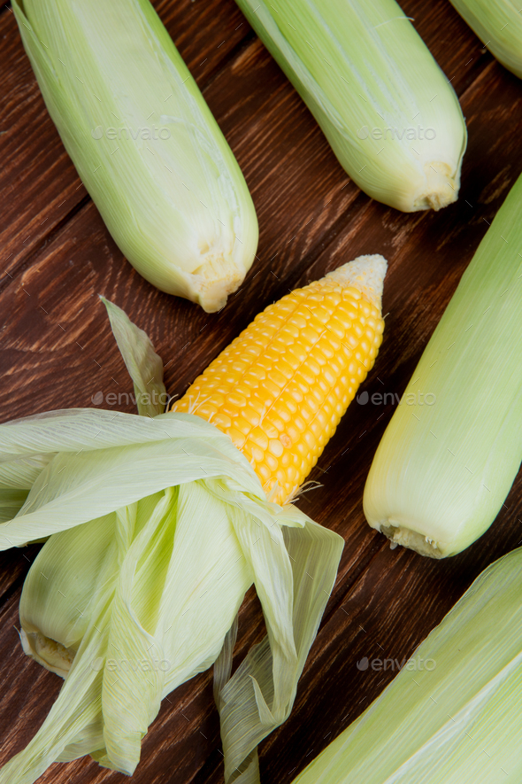 side view of corn cobs with shell on wooden background Stock Photo by ...