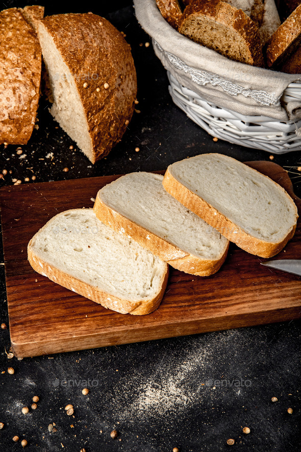 side view of breads as white, black, rye with cutting board on black ...