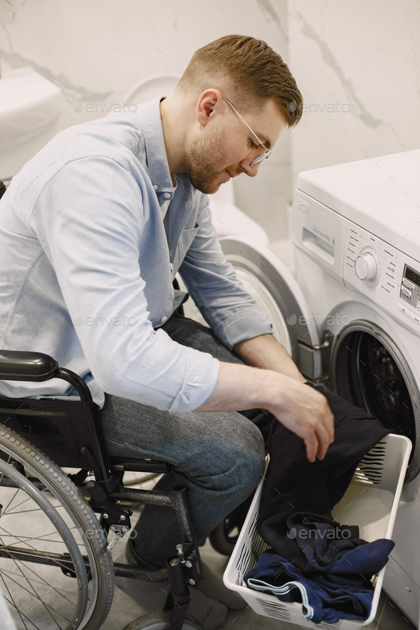 Impaired man in wheelchair put laundry in washing machine Stock Photo ...