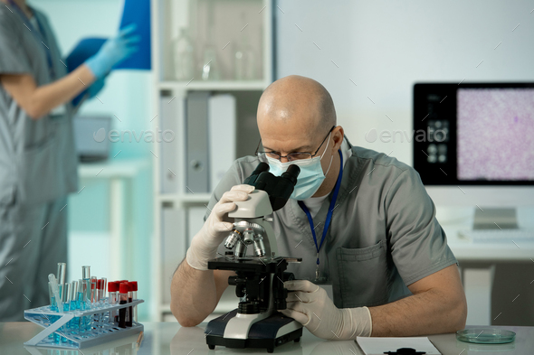 Concentrated lab worker analyzing blood cells Stock Photo by Pressmaster