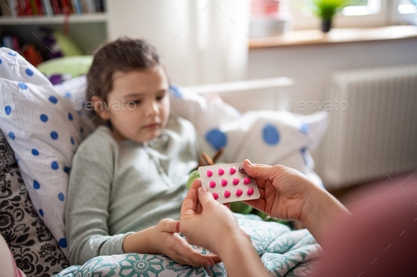 Mother looking after sick small daughter in bed at home, giving ...