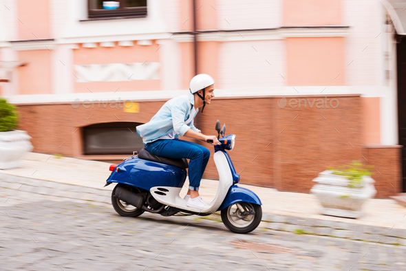 Scooter ride. Side view of young man in helmet riding scooter along the ...