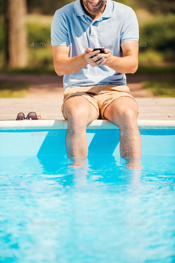 Man relaxing poolside. Cropped image of man sitting poolside and typing ...